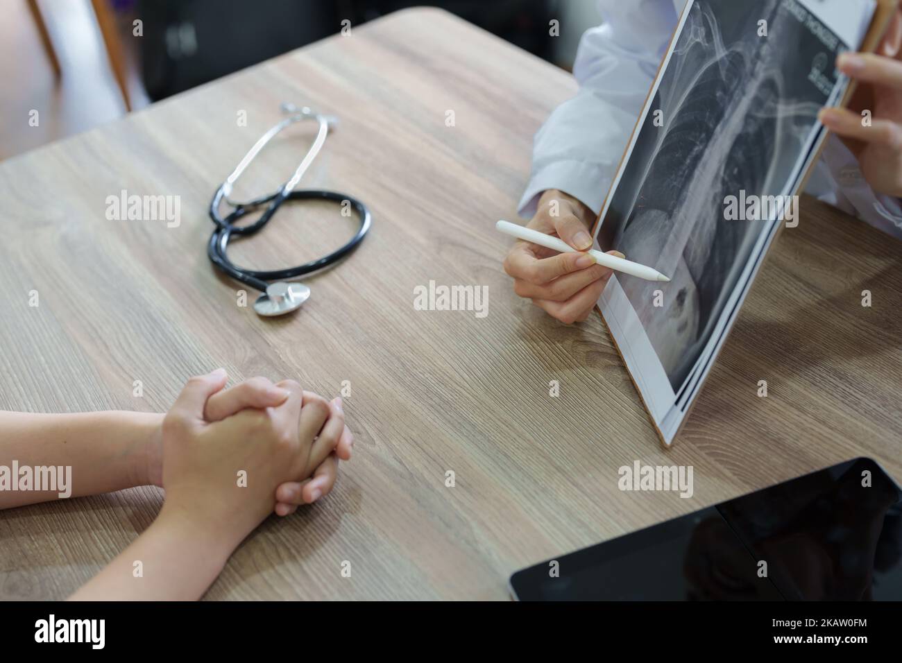 An Asian female doctor points to a patient x-ray film to explain the ...