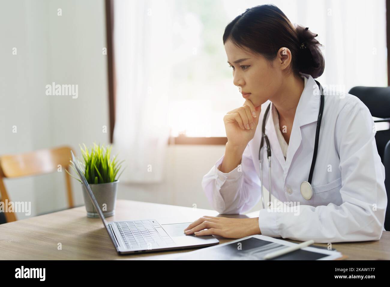 An Asian female doctor uses a computer while showing concern about ...