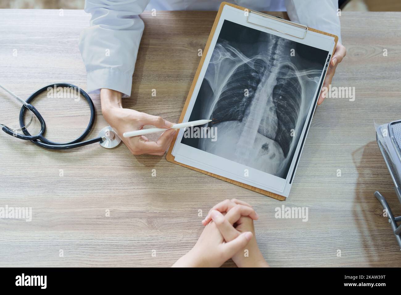 An Asian female doctor points to a patient x-ray film to explain the ...