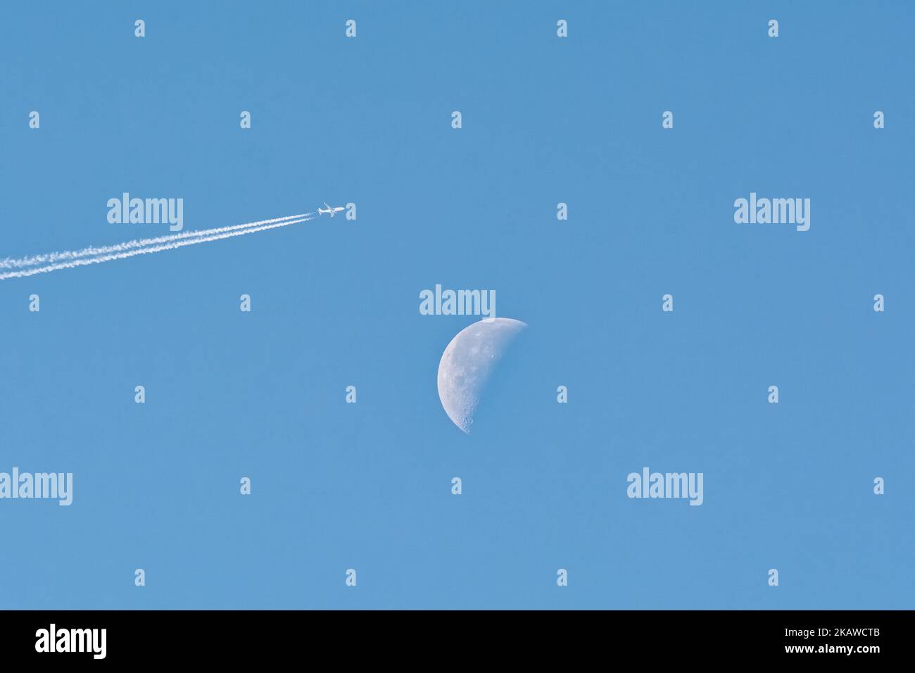 High flying passenger jet liner trailing contrail passing a half moon ...