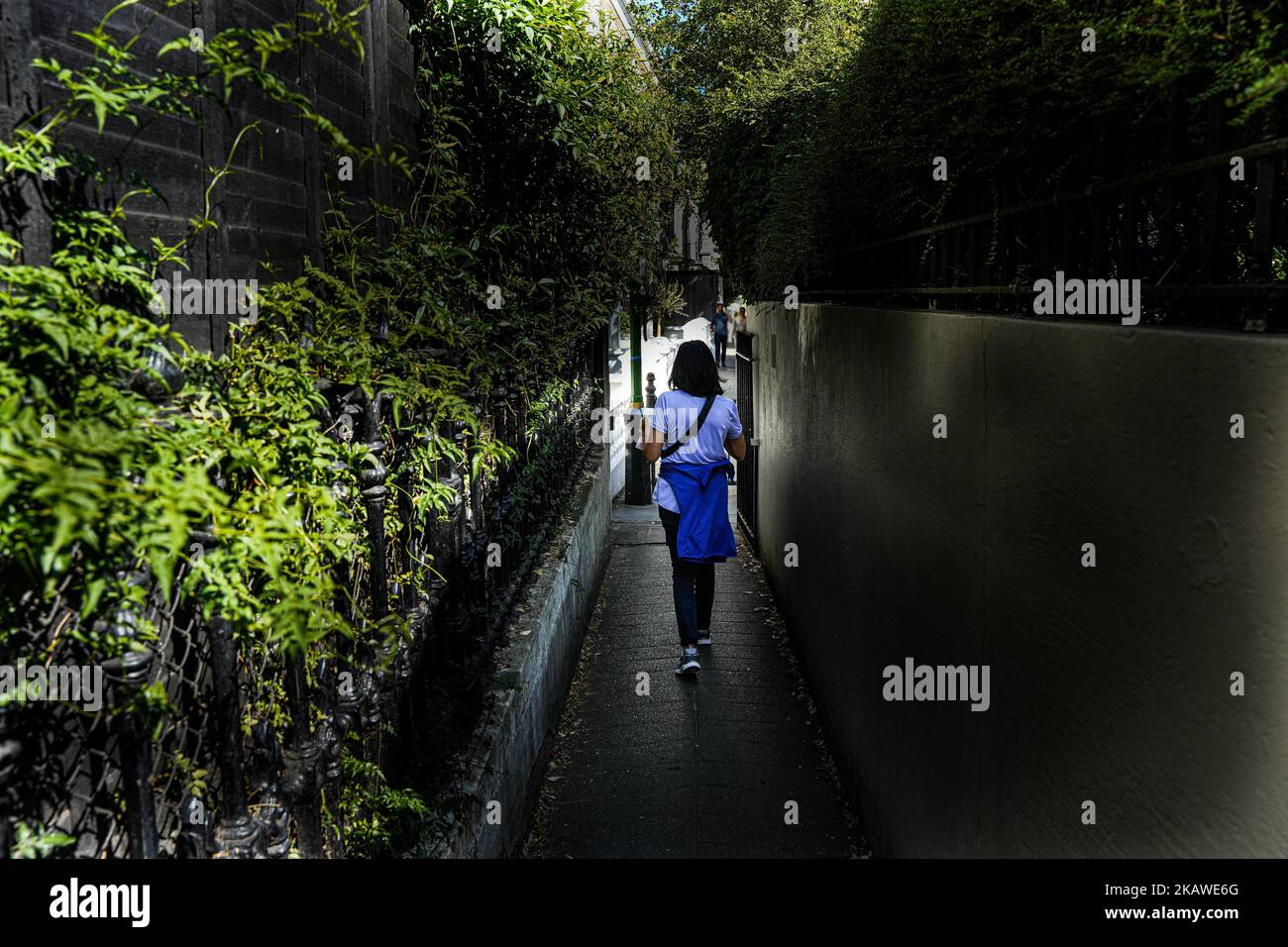 A girl walking through a corridor between houses covered with green ...