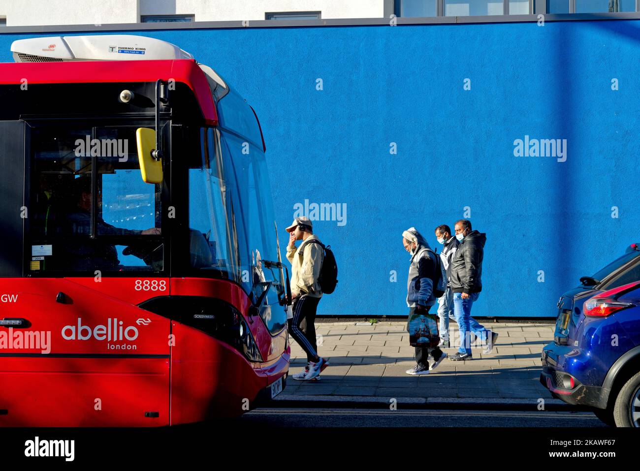Pedestrians walking past a blue painted hoarding with a red bus in ...