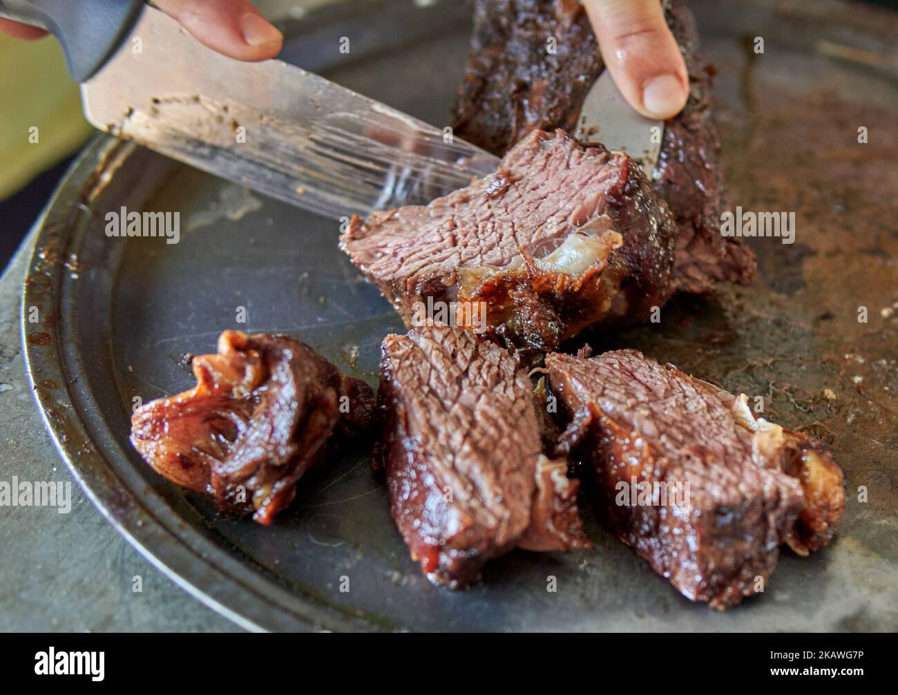 A closeup of hands cutting cooked delicious Argentinian barbeque meat ...
