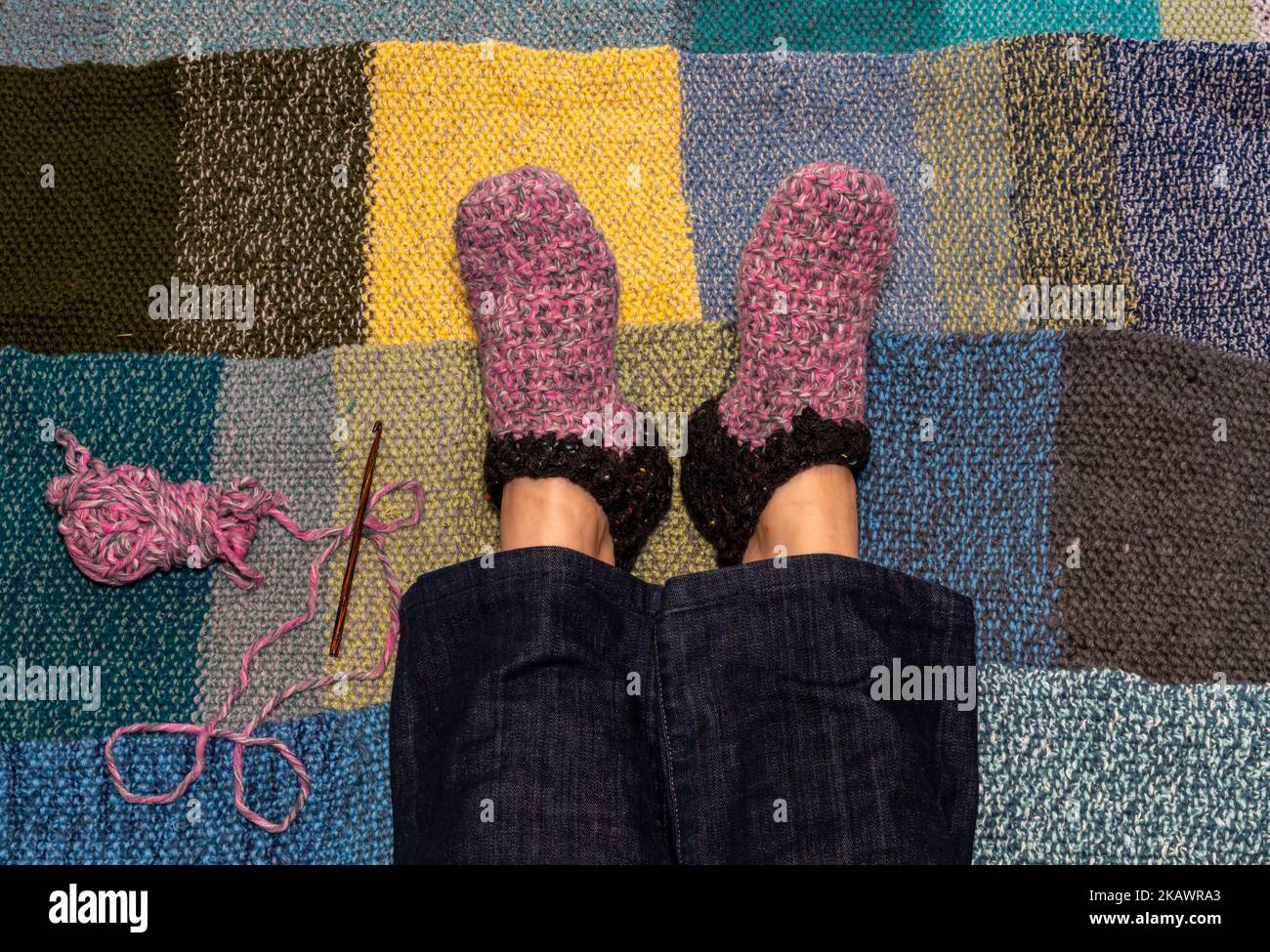 Woman feet wearing warm handmade slippers made of wool next to crochet ...