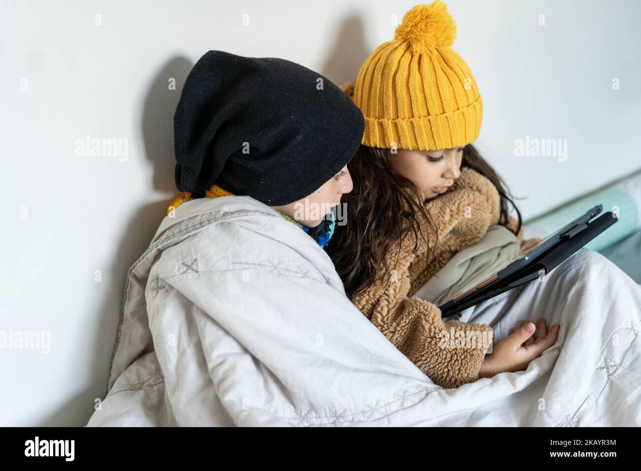 Children sitting in a bed in home in cold winter time. Siblings ...