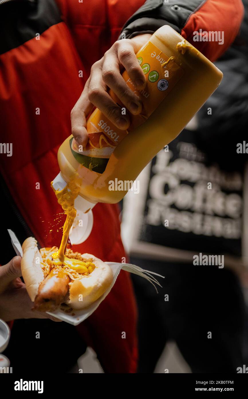 Close up someone pouring mustard onto their hotdog, sausage on a roll ...