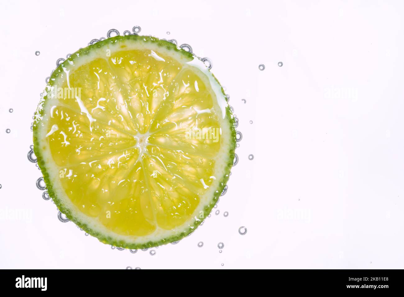 Macro photo of lime slice In water with bubbles isolated on white background. Freshness and ...