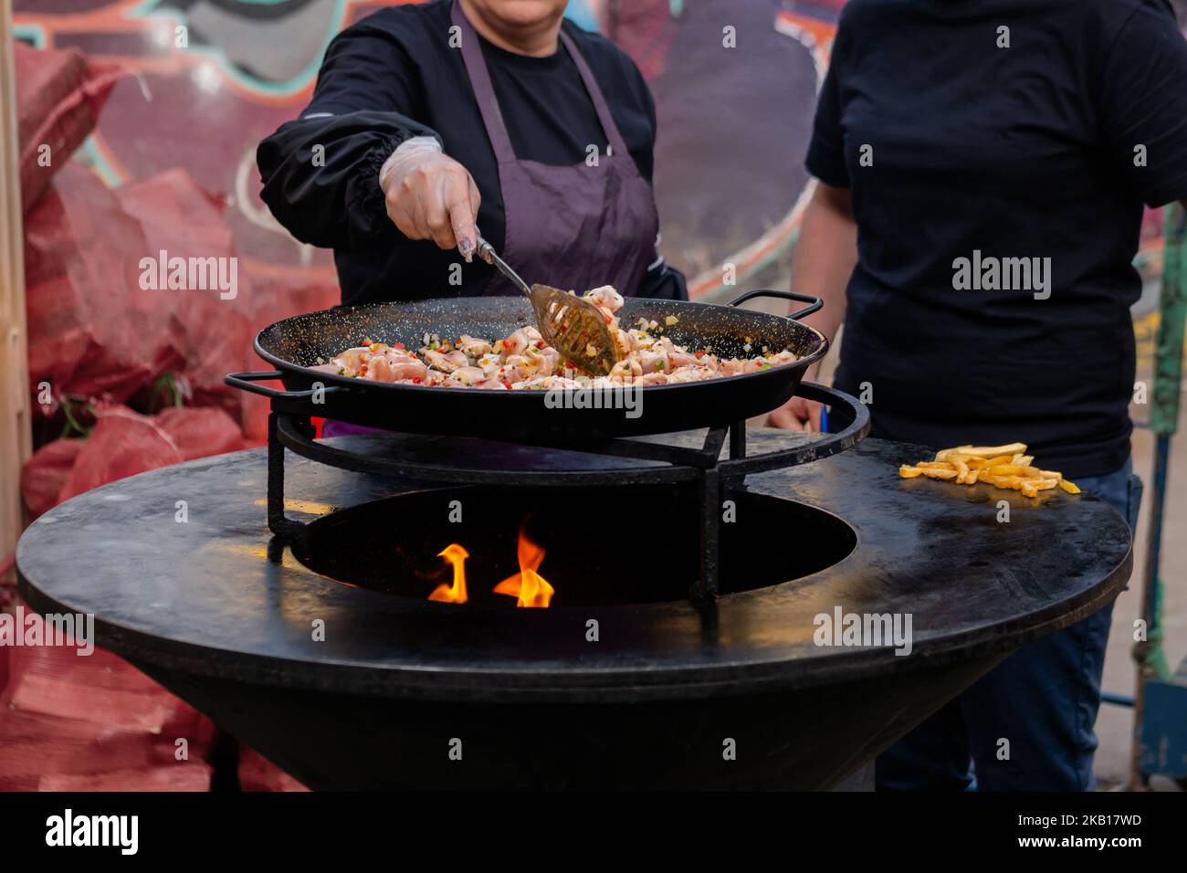 Woman chef cooking paella - fried chicken meat pieces, peppers, peas in ...