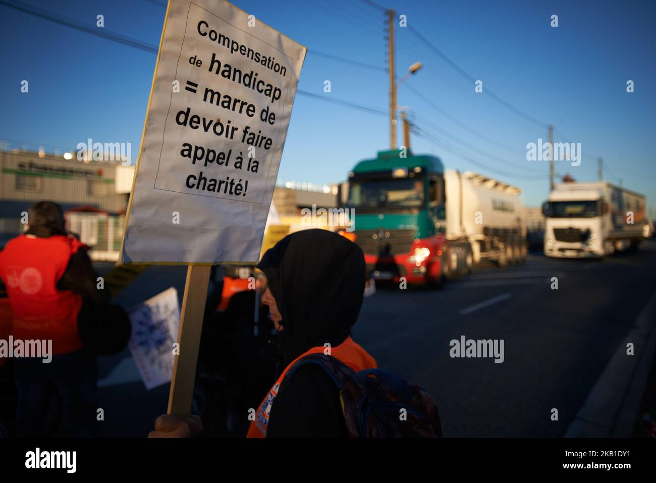 A woman on a wheelchair holds a placard reading 'Handicap compensation ...