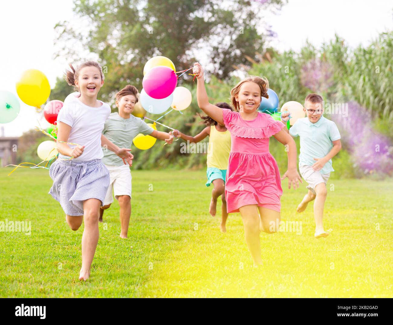 Happy tween friends with balloons chasing each other on green meadow ...