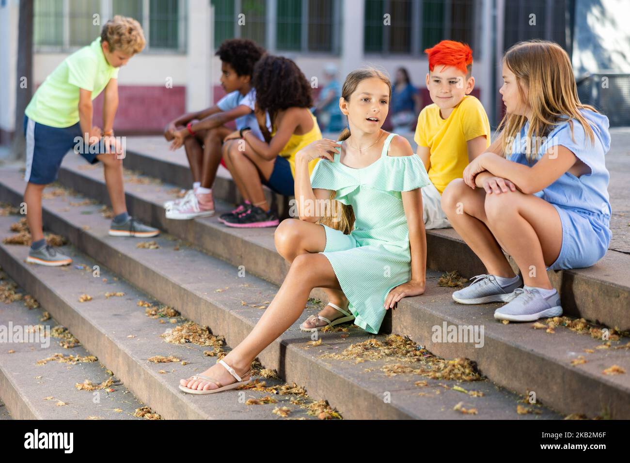 Positive tweenagers friendly blabbing while sitting on steps outdoors ...