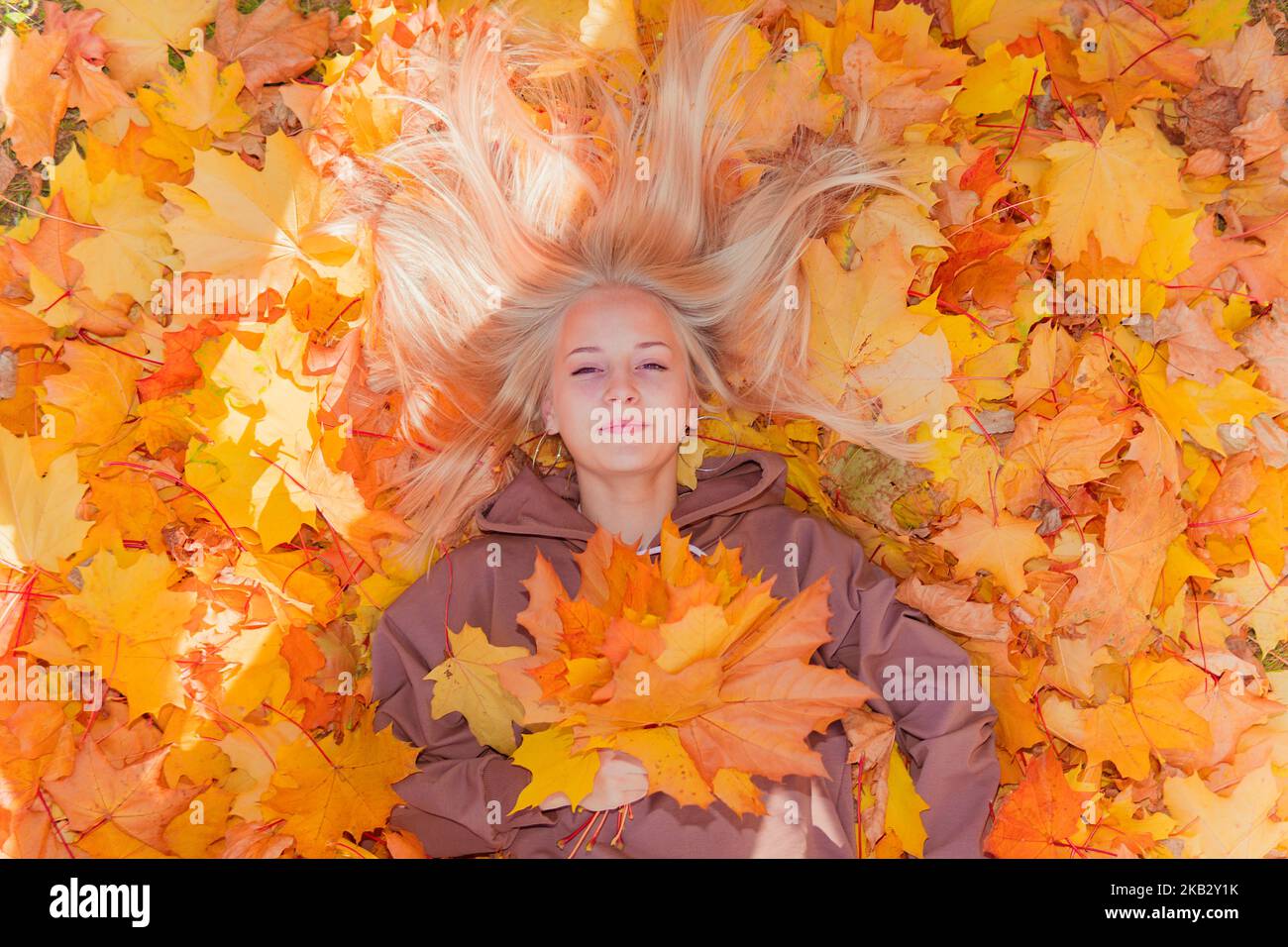 blonde teenager girl lies in yellow autumn foliage and smiles Stock ...