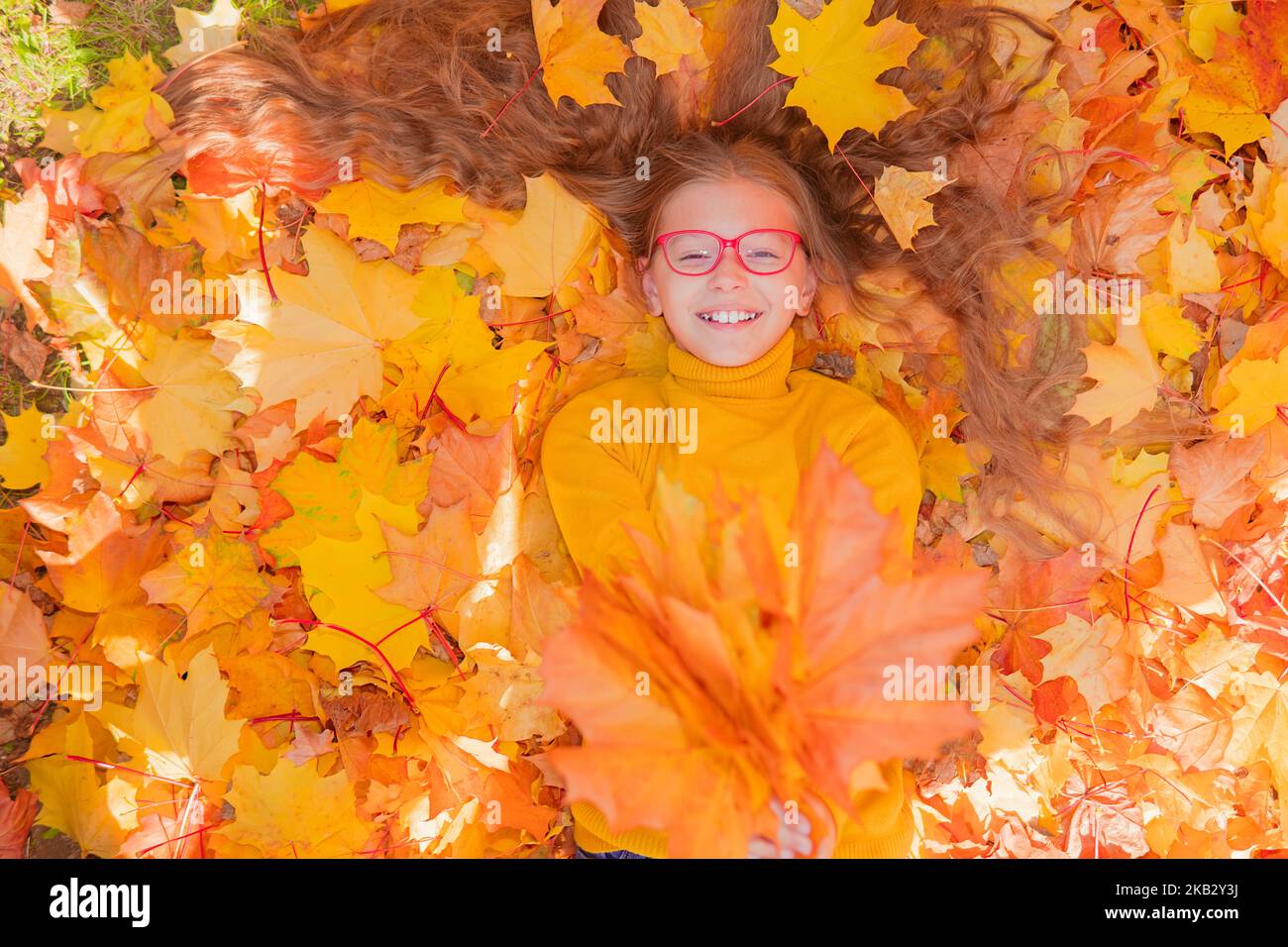 a teenage girl in red glasses lies in yellow autumn foliage and smiles ...