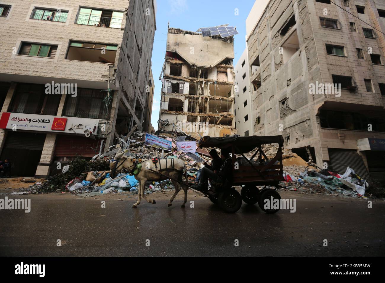 Palestinian men ride a donkey cart past the remains of a building that ...