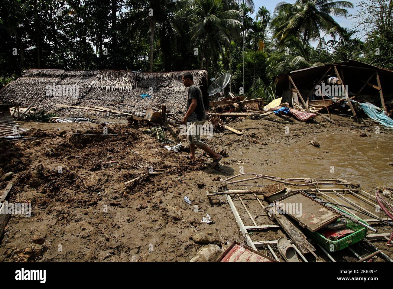 A man collects debris from a house damaged after a flood caused by ...