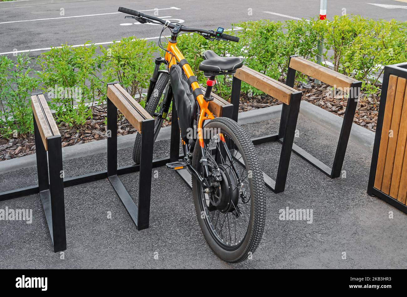 Electric mountain bike parked on a public bike rack next to green hedge ...