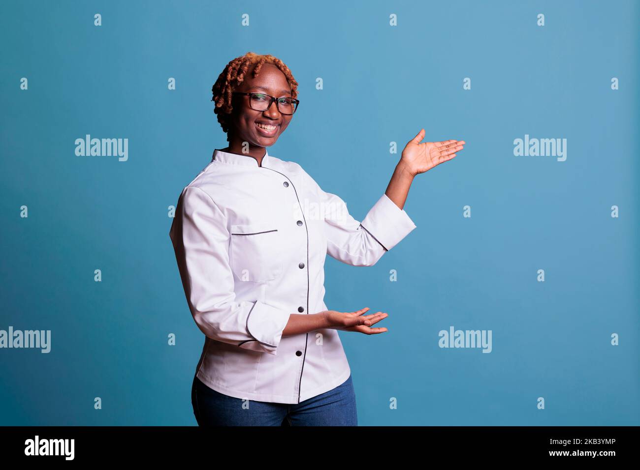 Smiling professional cook in kitchen uniform holding imaginary product ...