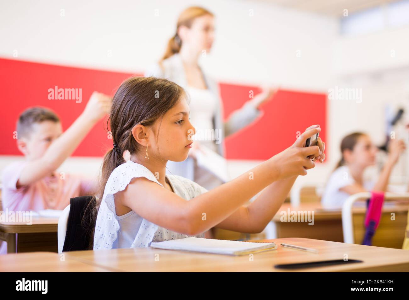 Schoolgirl using phone in classroom during lesson Stock Photo - Alamy