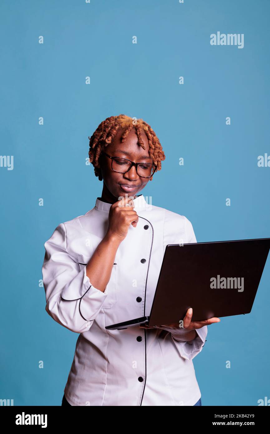 Female chef dressed in work uniform using laptop to read customer ...