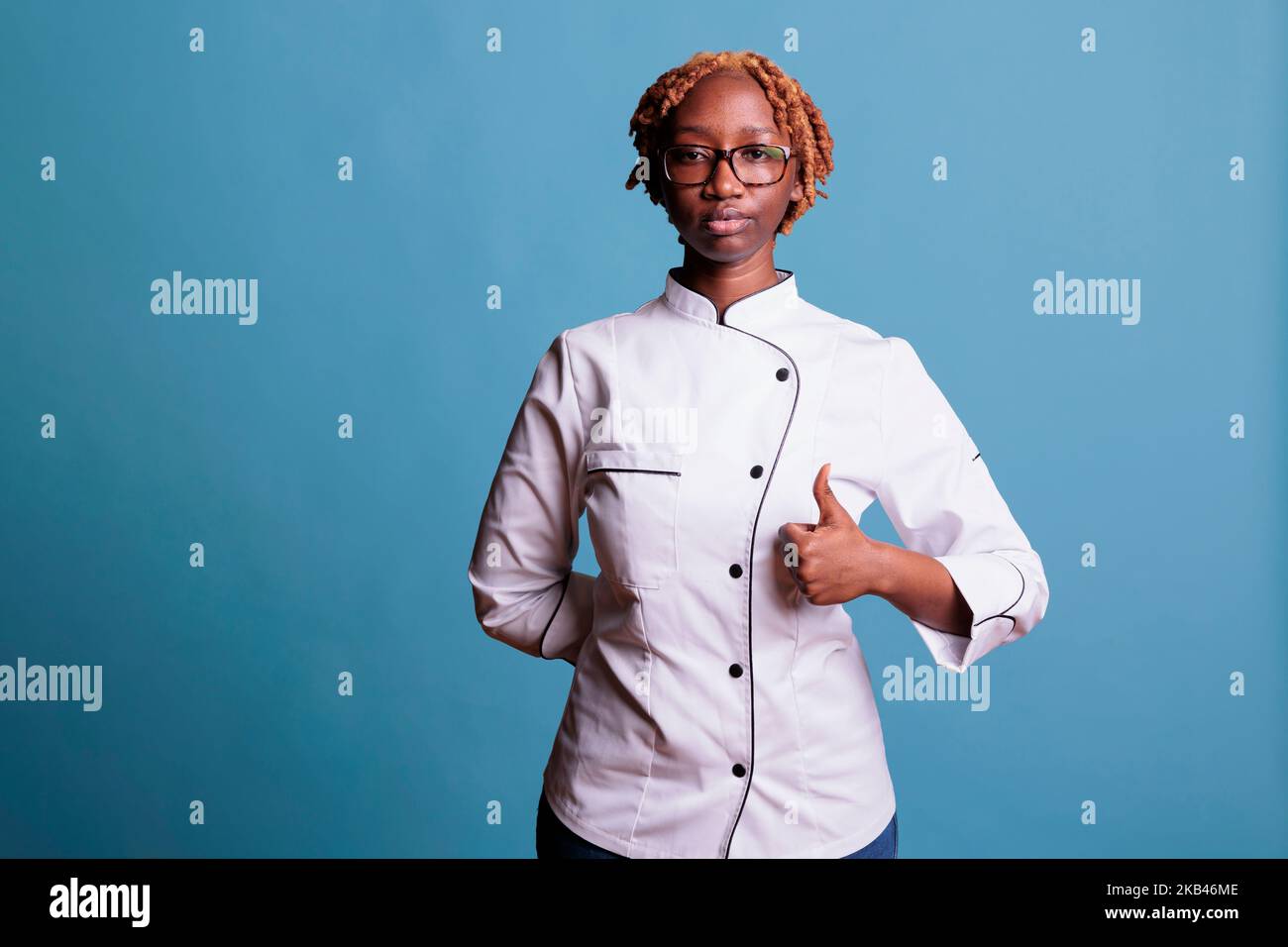 Serious African American female chef standing with thumbs up looking at ...