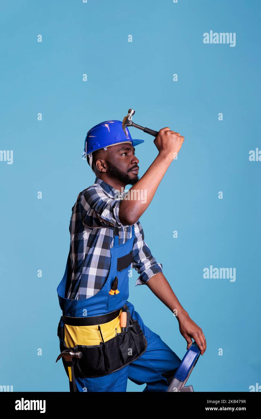 African American Construction Worker On Ladder Using Hammer To Drive