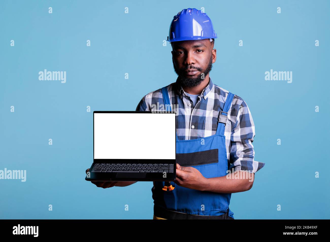Serious builder looking at camera holding laptop with blank screen for ...