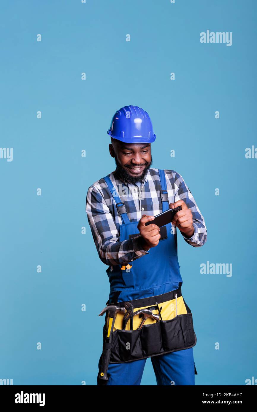 Contractor playing video games with mobile phone against light blue ...