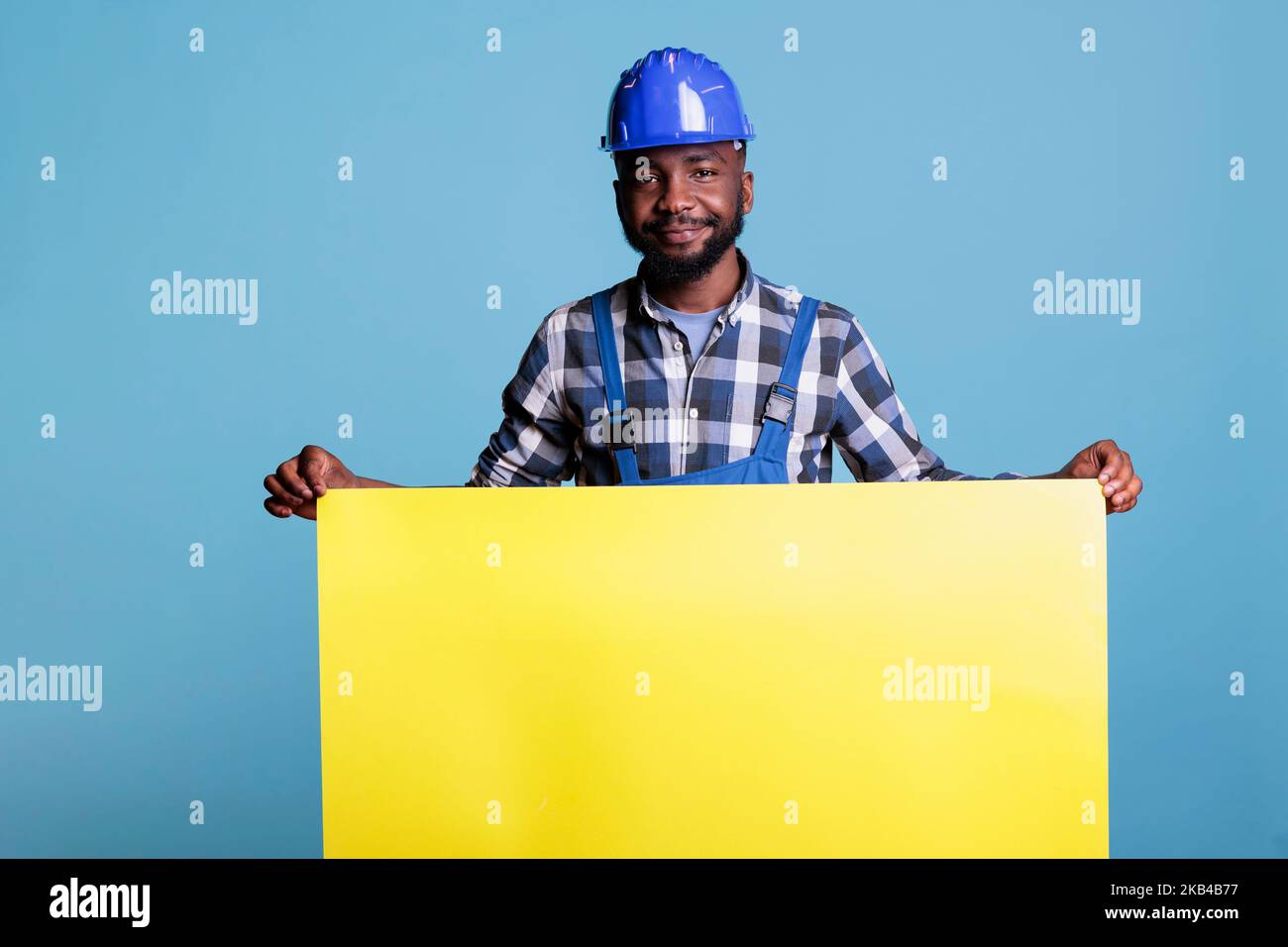 Optimistic builder in hard hat holding large empty yellow banner for ...