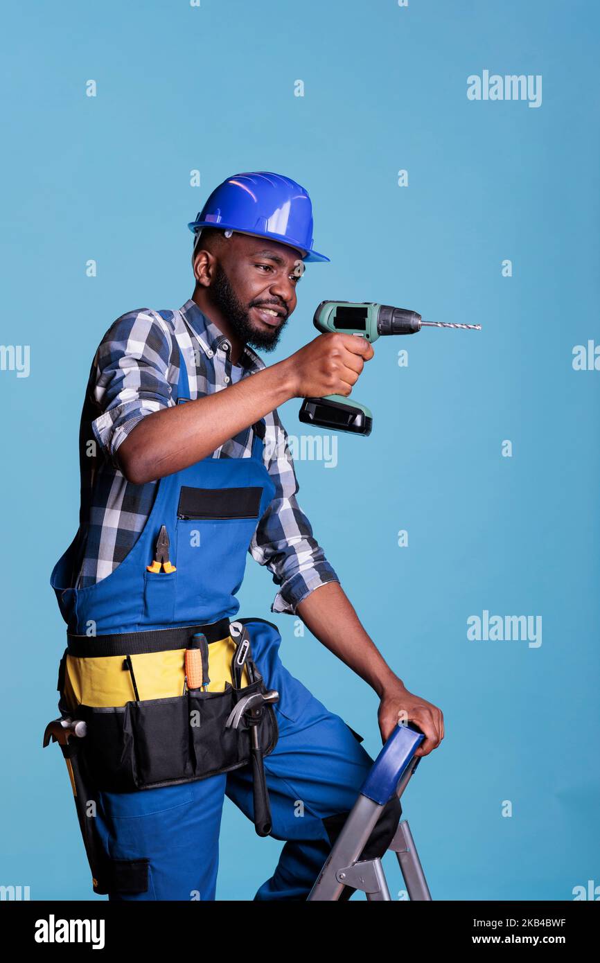 Construction worker on ladder drilling wall with cordless drill doing ...