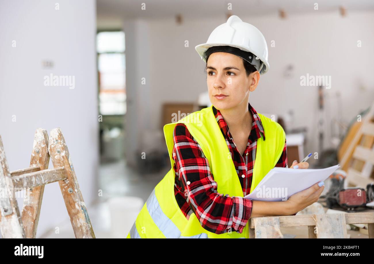 Focused young female civil engineer making notes at construction site ...