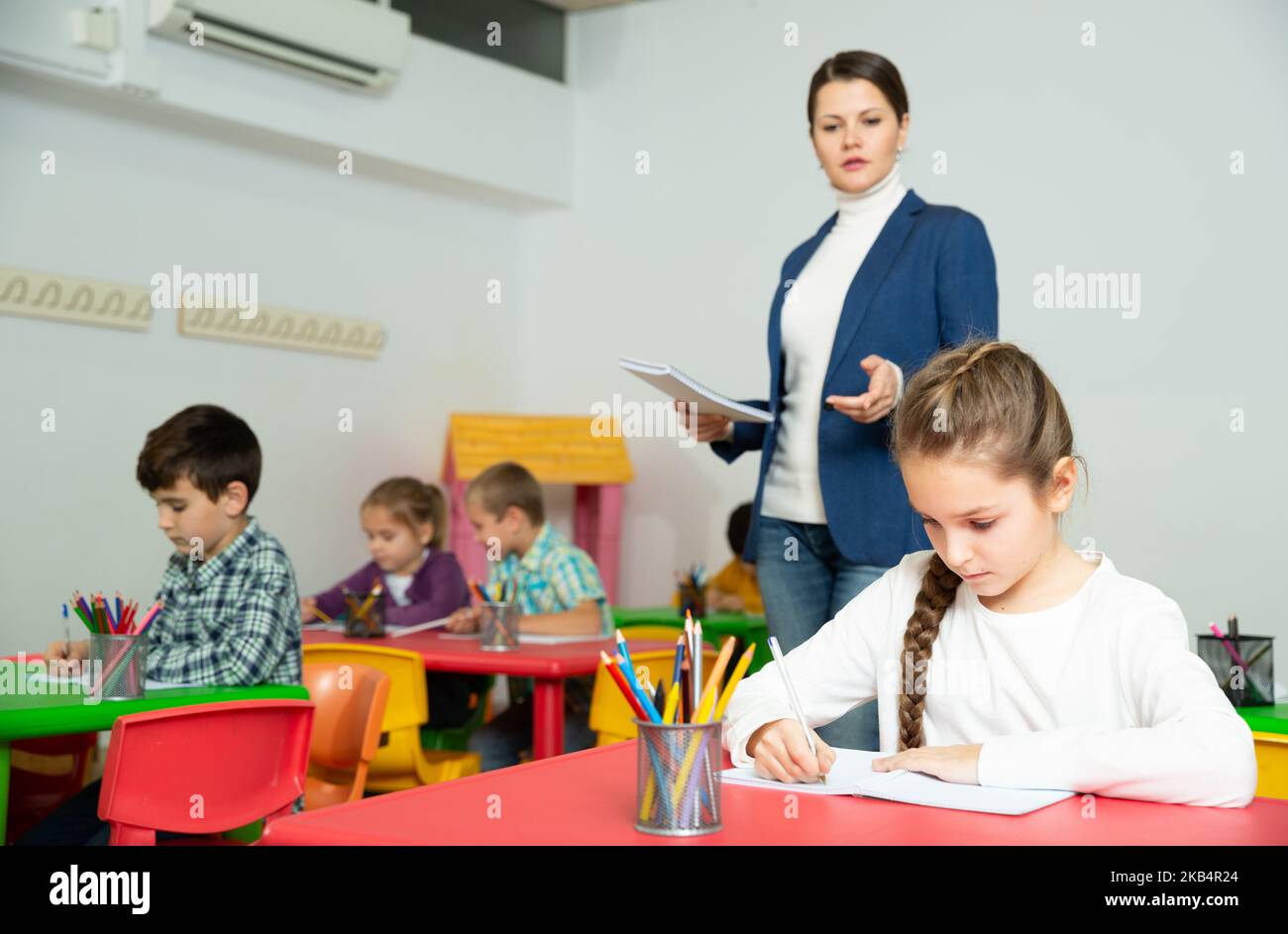 Friendly teacher woman helping girl during lesson in schoolroom Stock ...