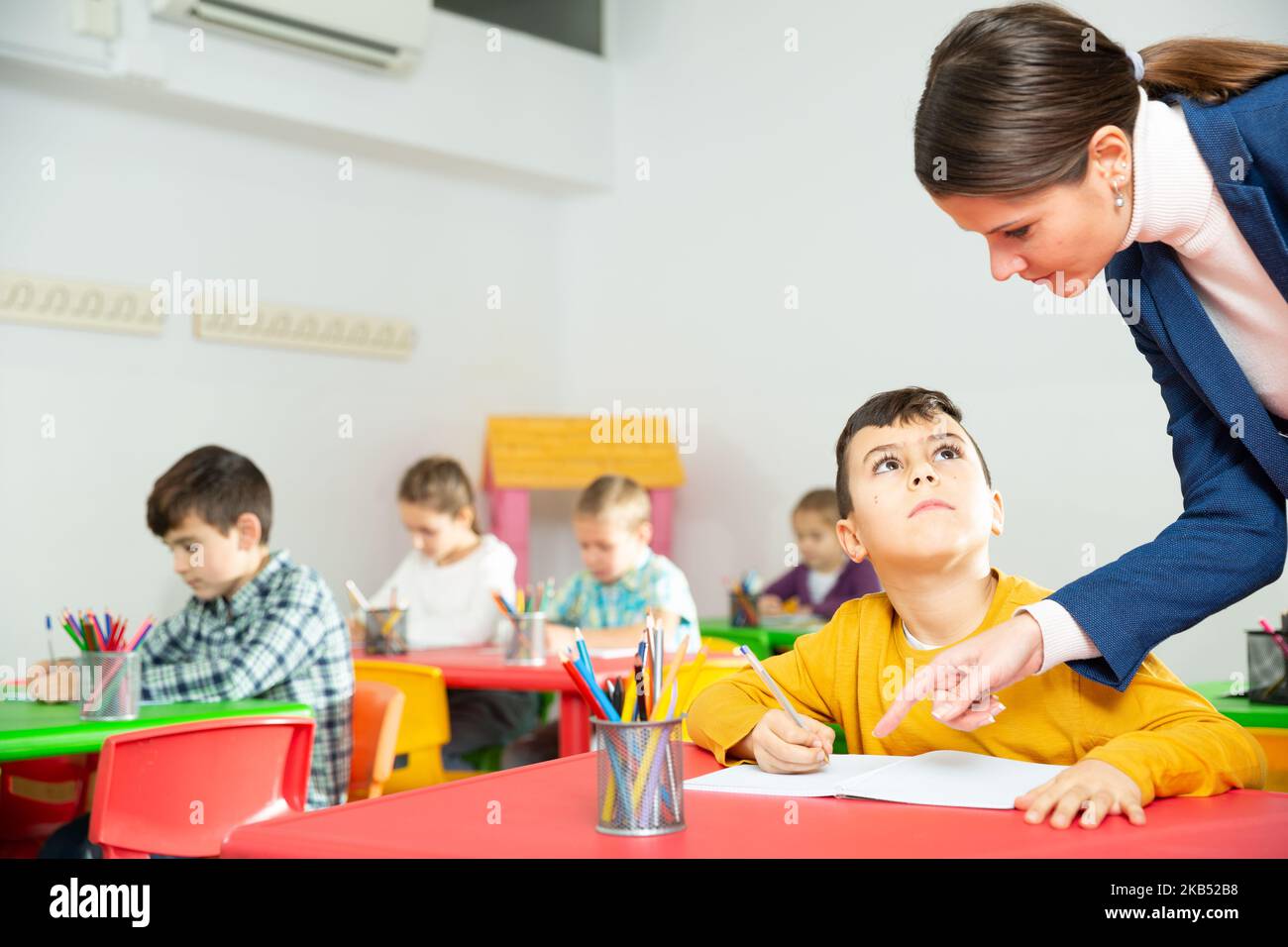 Friendly teacher woman helping boy during lesson in schoolroom Stock ...
