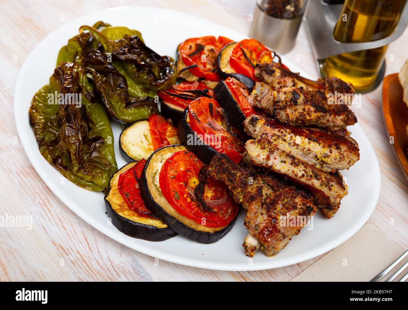 Grilled pork ribs rack garnished on white plate with eggplant; tomatoes ...