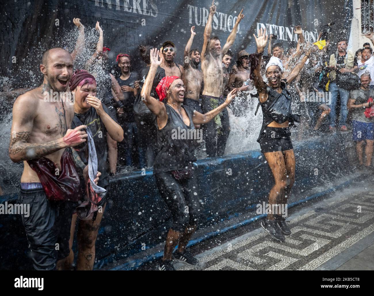 People covered with black grease play with water as they celebrate the ...