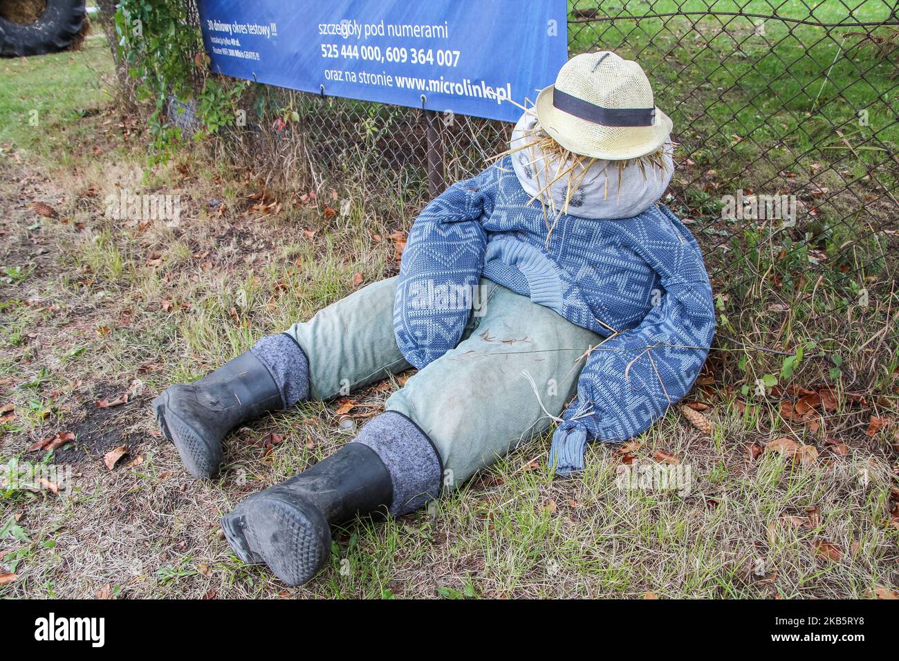 Straw installations in the shape of drunk farmer lying under the fence ...