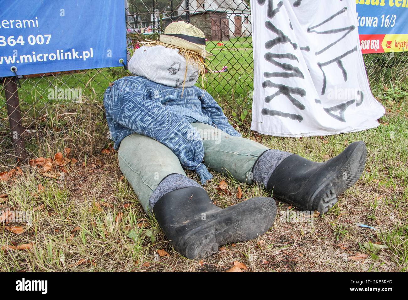 Straw installations in the shape of drunk farmer lying under the fence ...