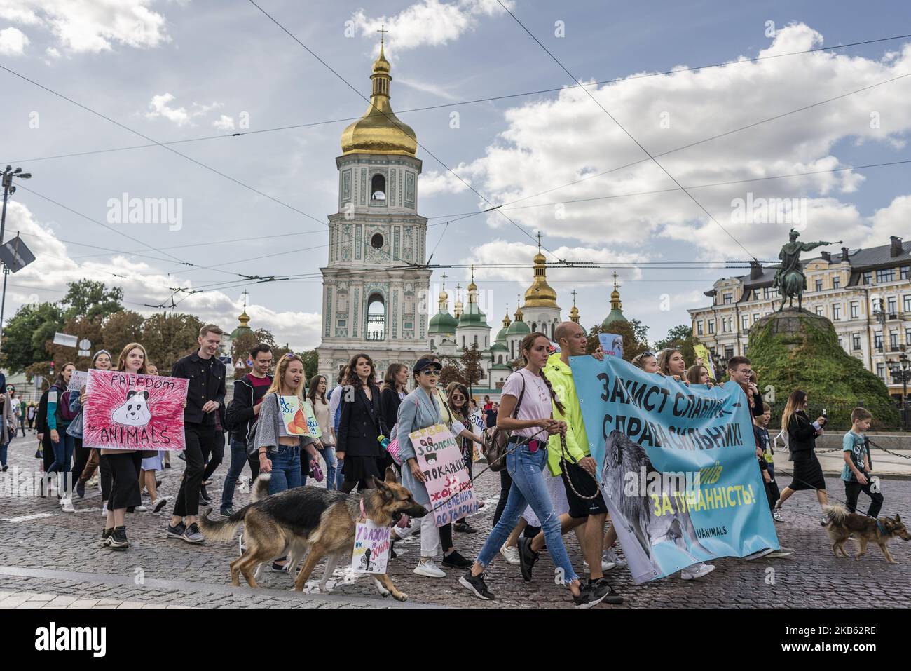 People with their dogs stand near a placard depicting lion and signed ...