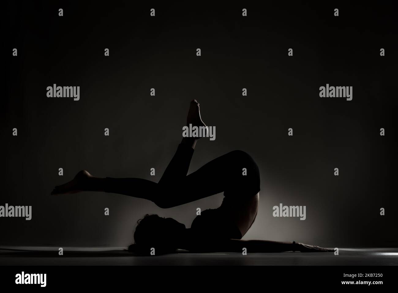 Fit ballerina girl lying and stretching practicing yoga poses. Side lit ...