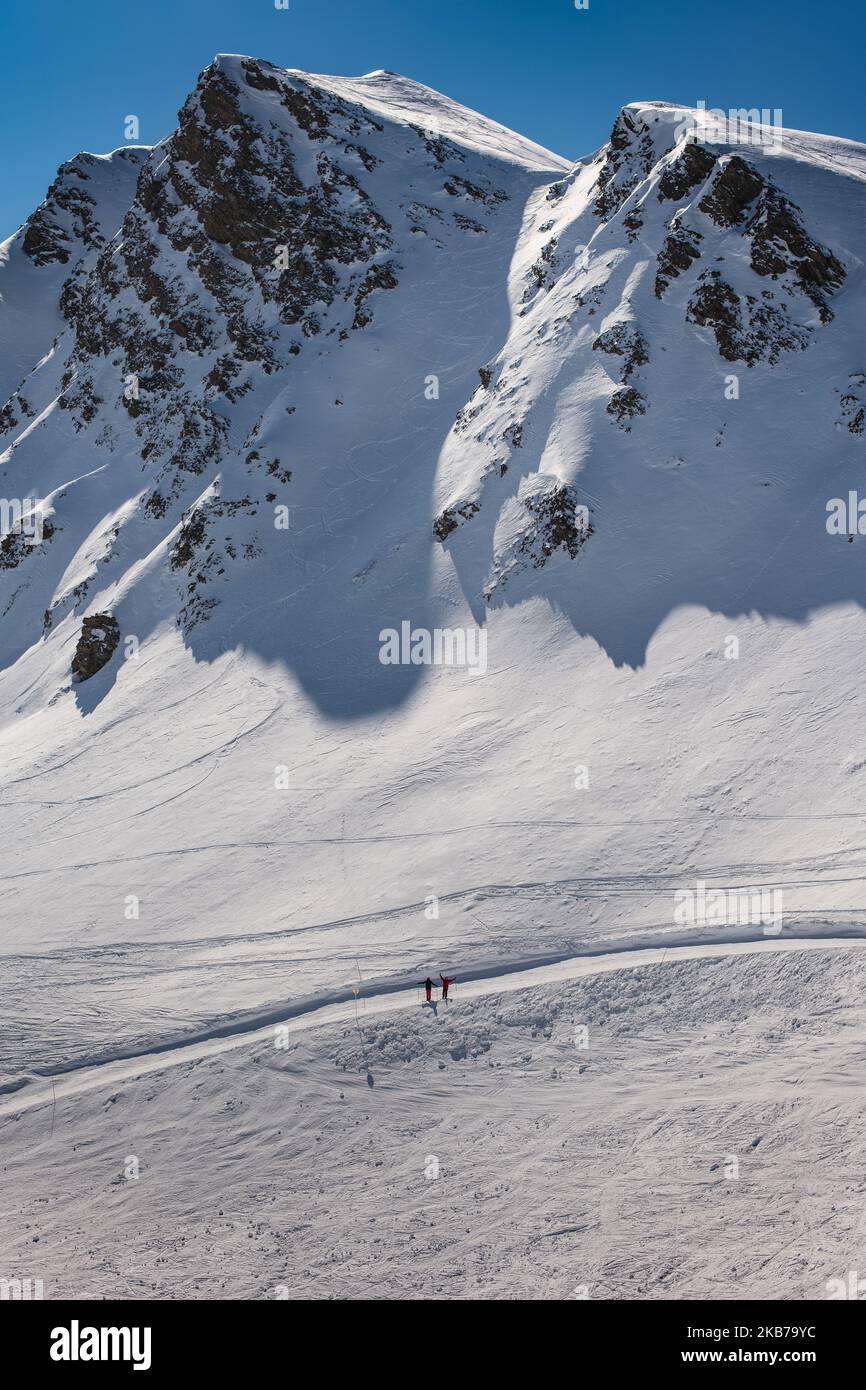 Two skiers engulfed by the size of the mountains around piste ski run ...