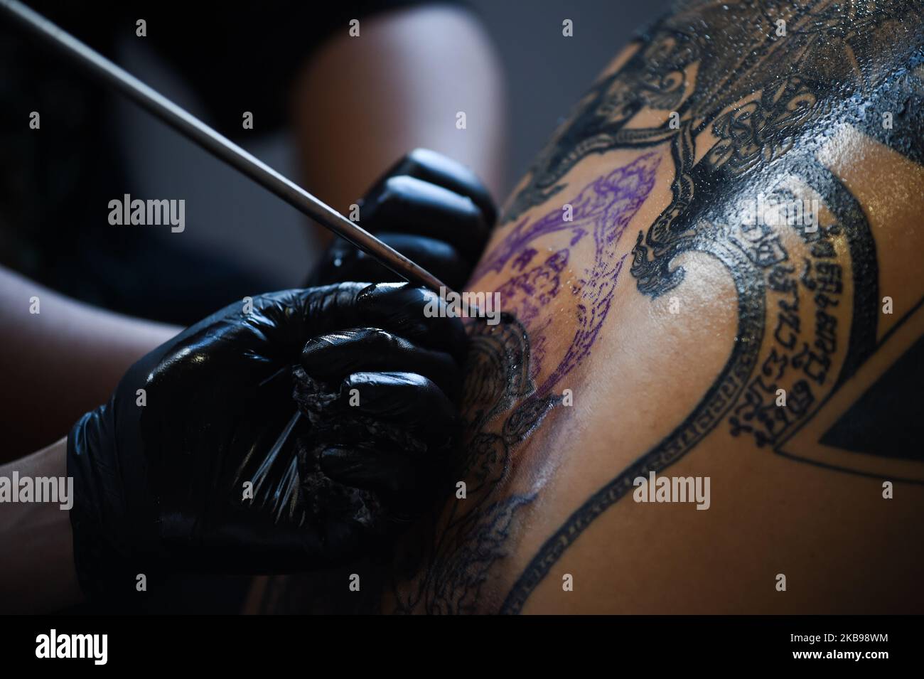 A man gets a tattoo uses a traditional needle on the back in at the ...