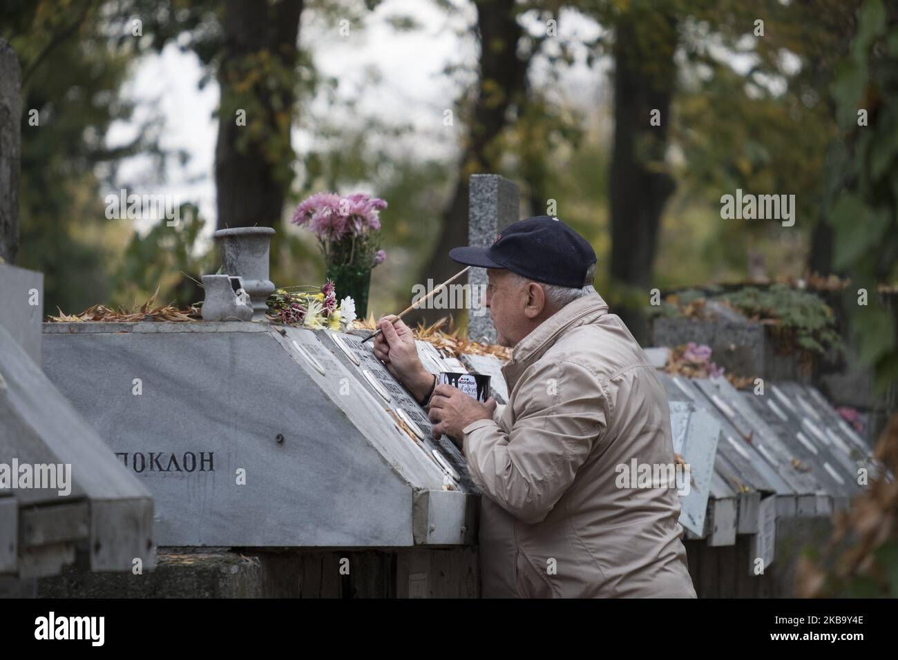 A man touches up the name of his relative on a burial stone during All ...