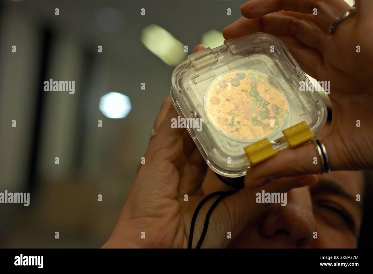 A woman looks at the prototype sapphire disk with a magnifying glass ...