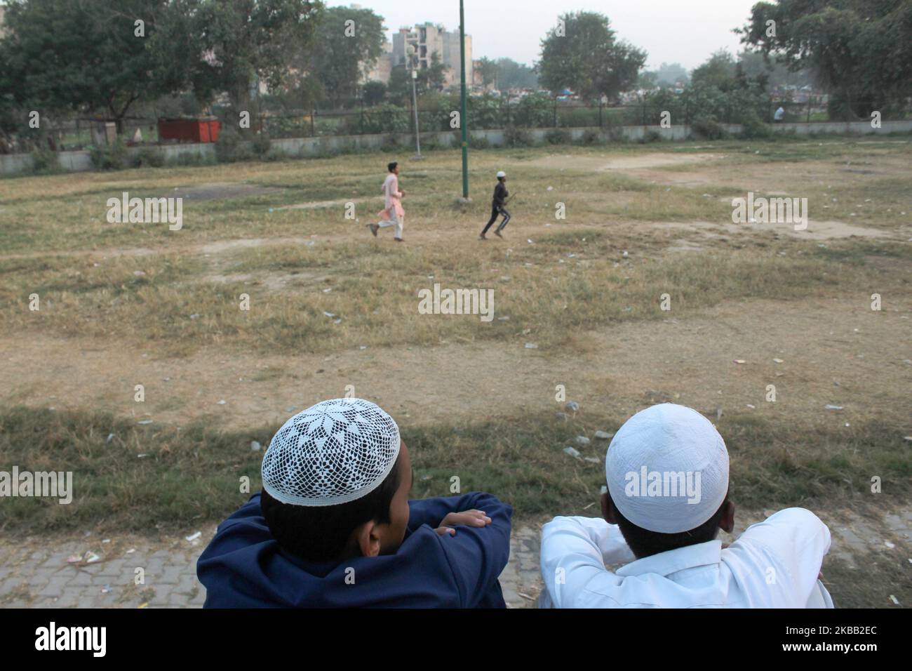 Two boys watch other boys playing a game of 'Gilli Danda' at a local ...