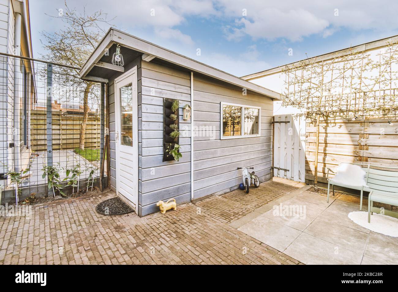 Neat paved patio with sitting area and small garden near wooden fence ...