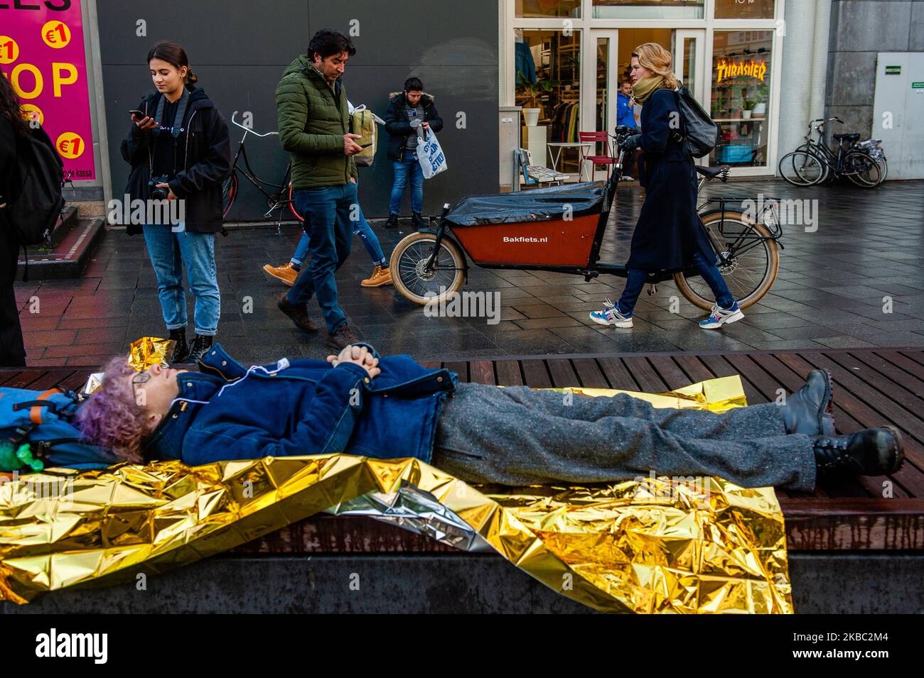 An XR activist is lying on a bench while people is passing by, during ...