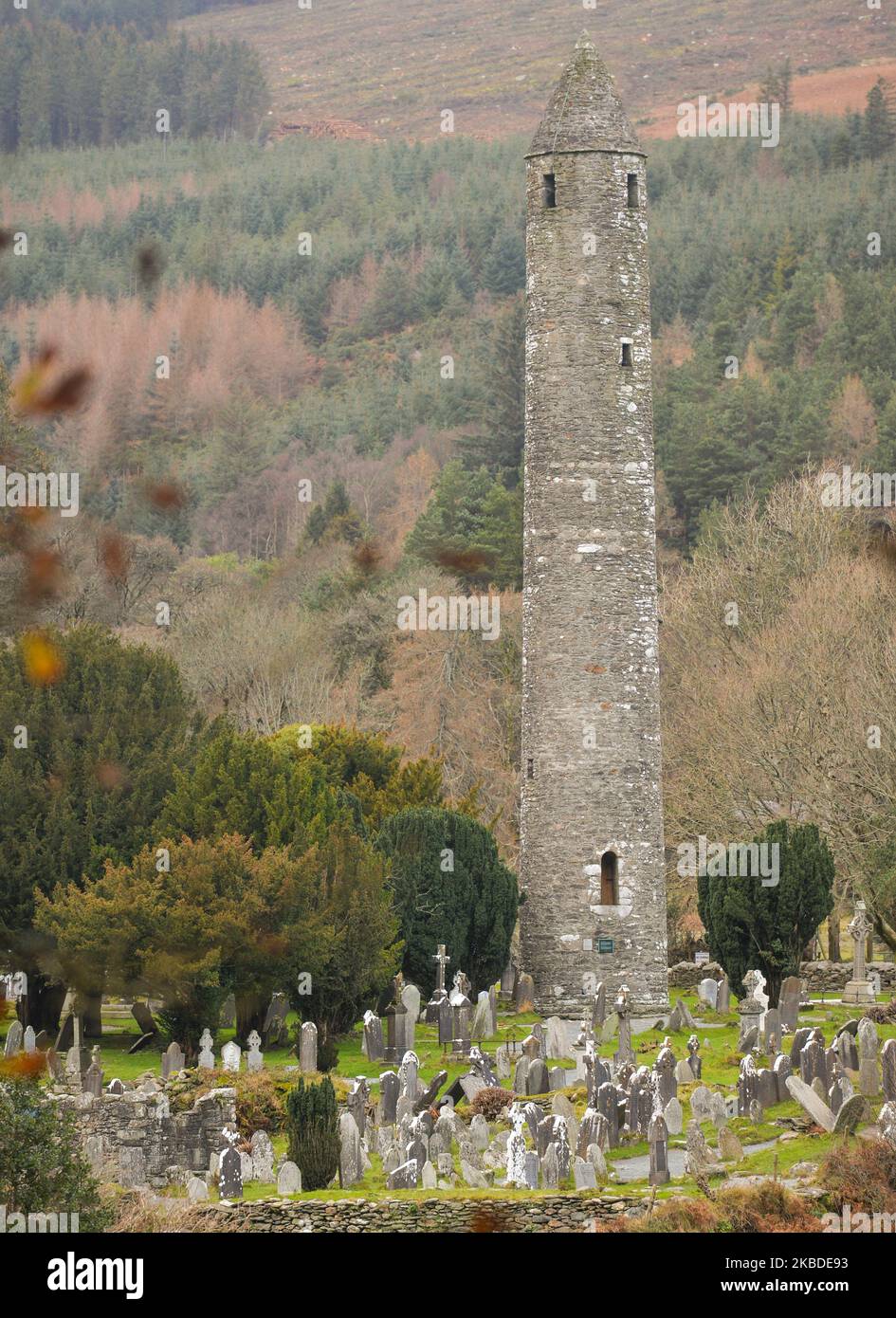 A view of an Irish round tower, tombstones and Celtic crosses inside an ...