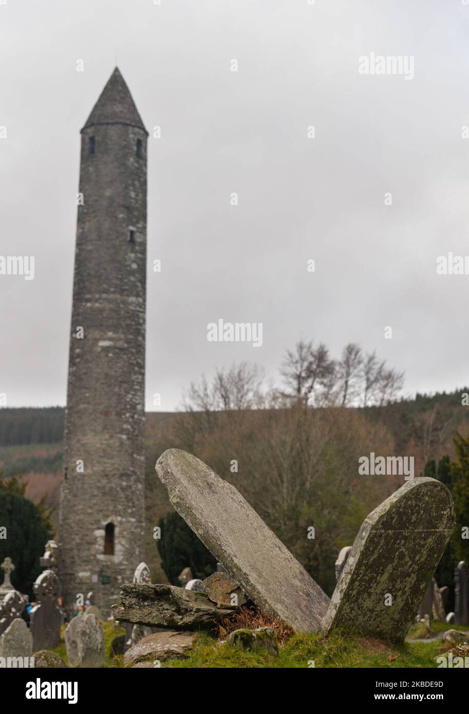 A view of an Irish round tower, tombstones and Celtic crosses inside an ...