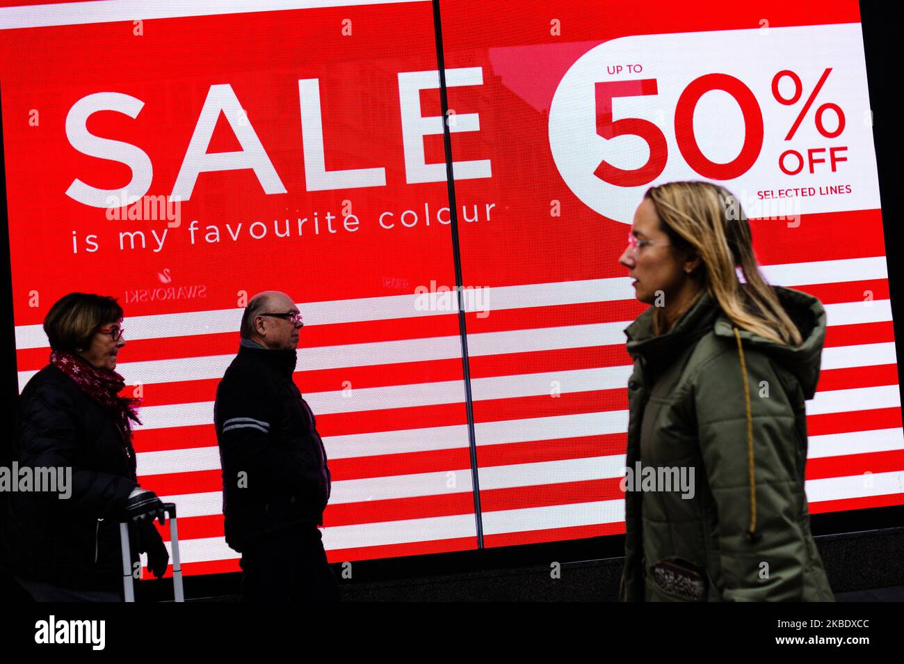 People walk past sales signs on a digital display in the window of ...