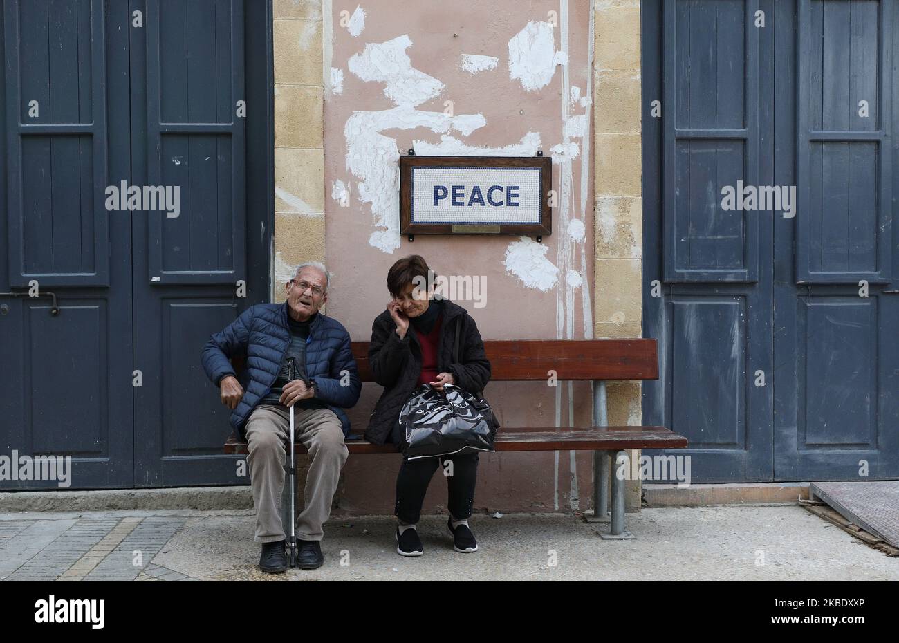 Man and woman sitting on a bench under a sign reading 'Peace' next to ...