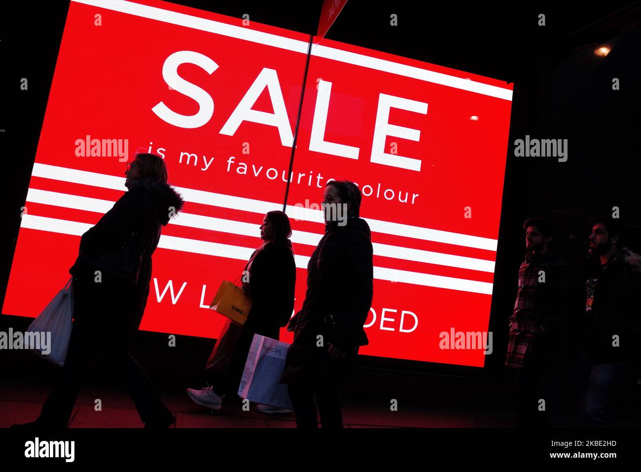 People walk past a sales sign on a digital display in the window of ...